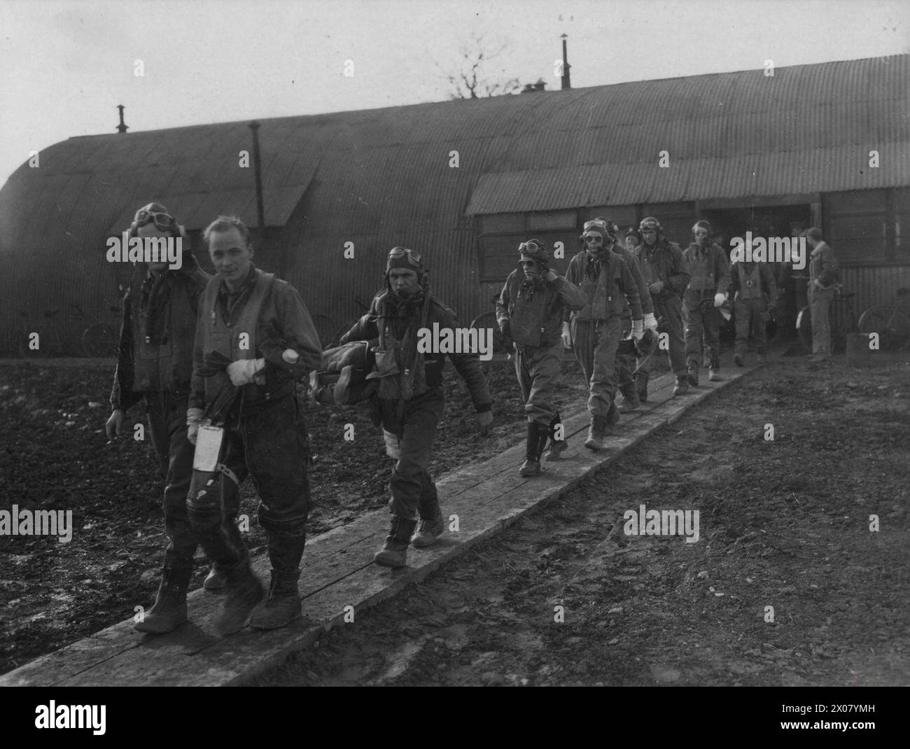 Pilots of the 55th Fighter Group, Eighth Air Force, cross duckboards ...