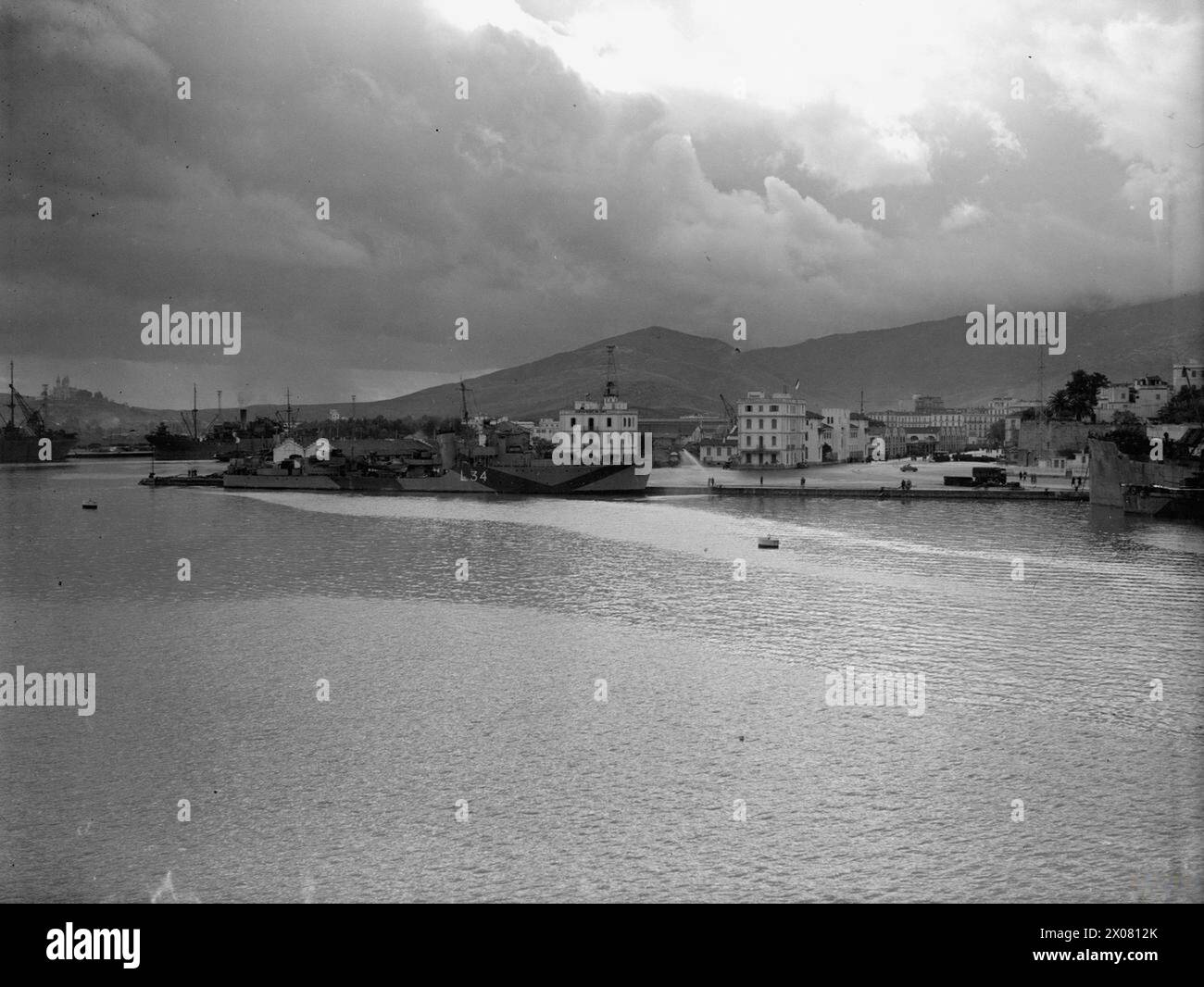 HMS Bicester, a destroyer, is alongside a jetty in Bona dockyard ...