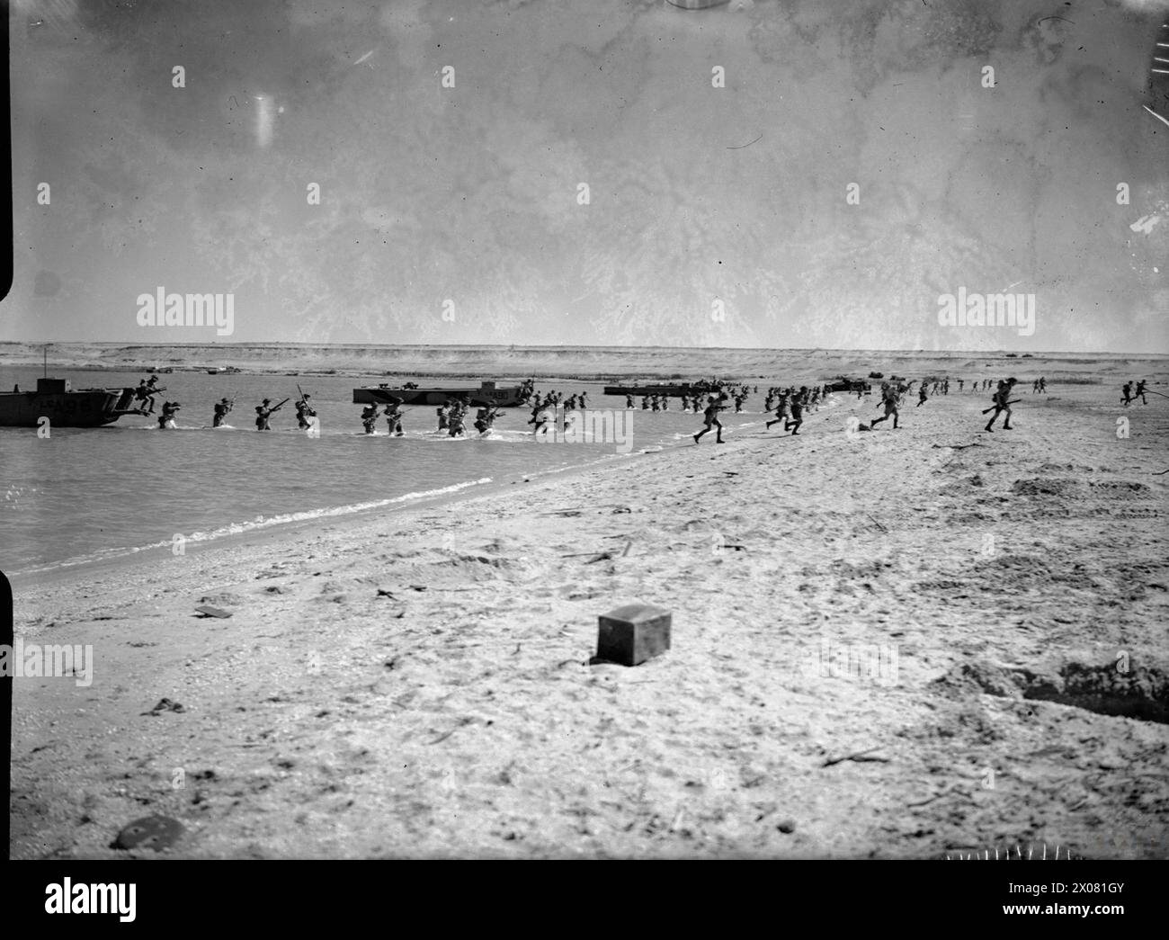 Army assault troops land from invasion craft while naval beach parties ...
