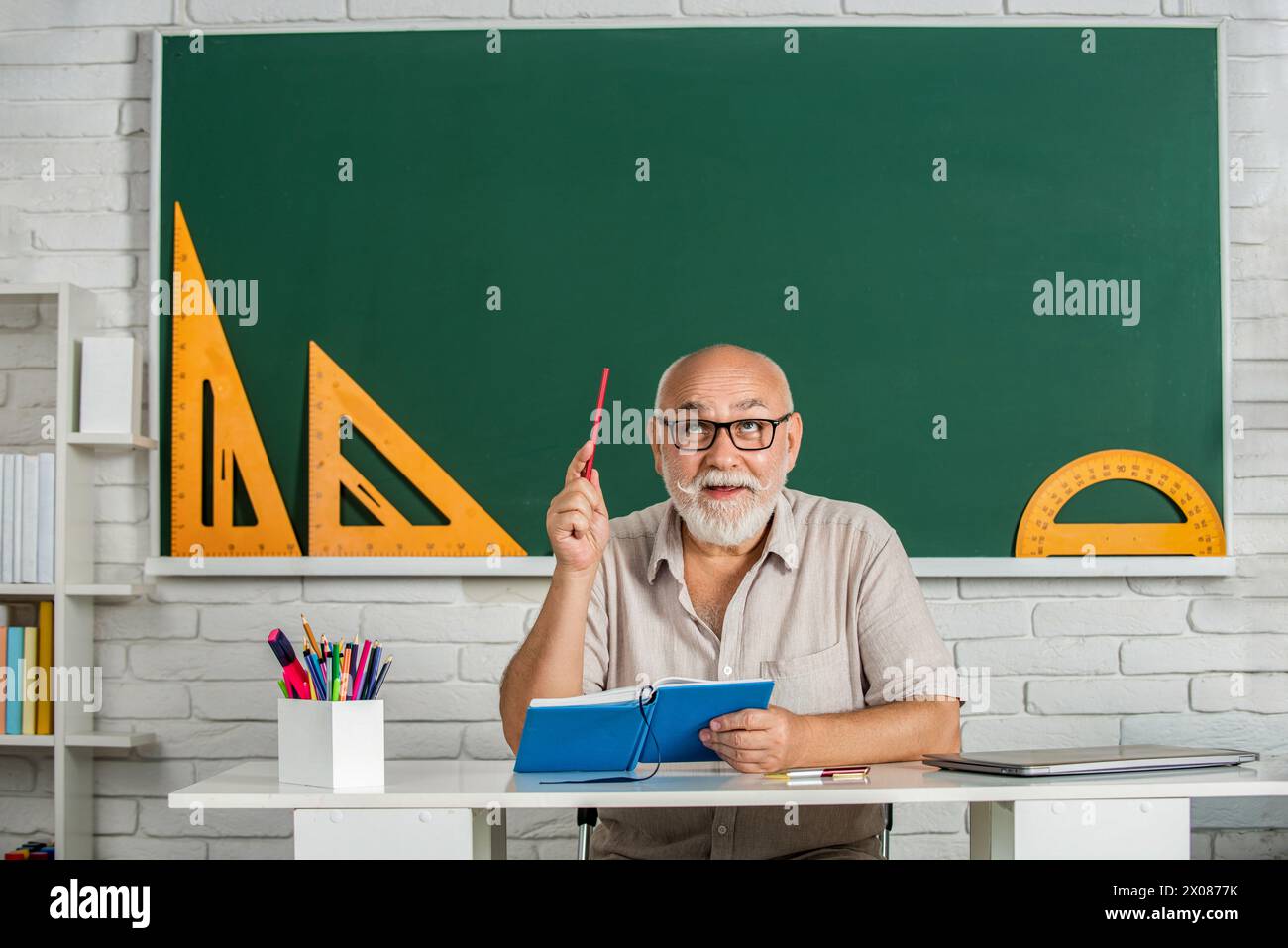 Smiling man in glasses sit at desk. Old man teachers on green board ...