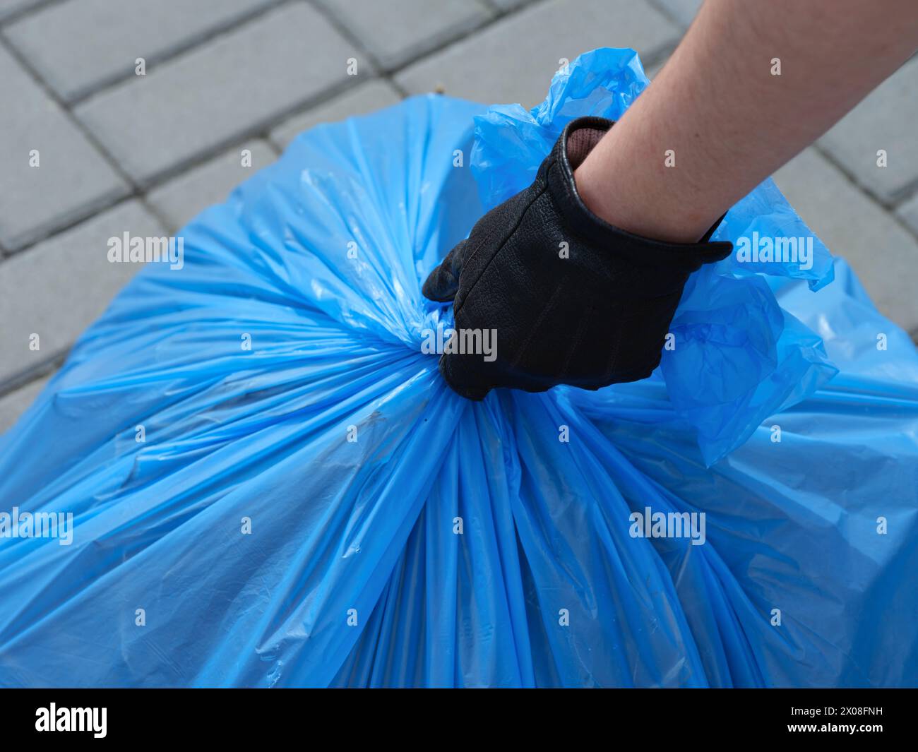A close-up shot of a person hand taking a blue garbage bag full of ...