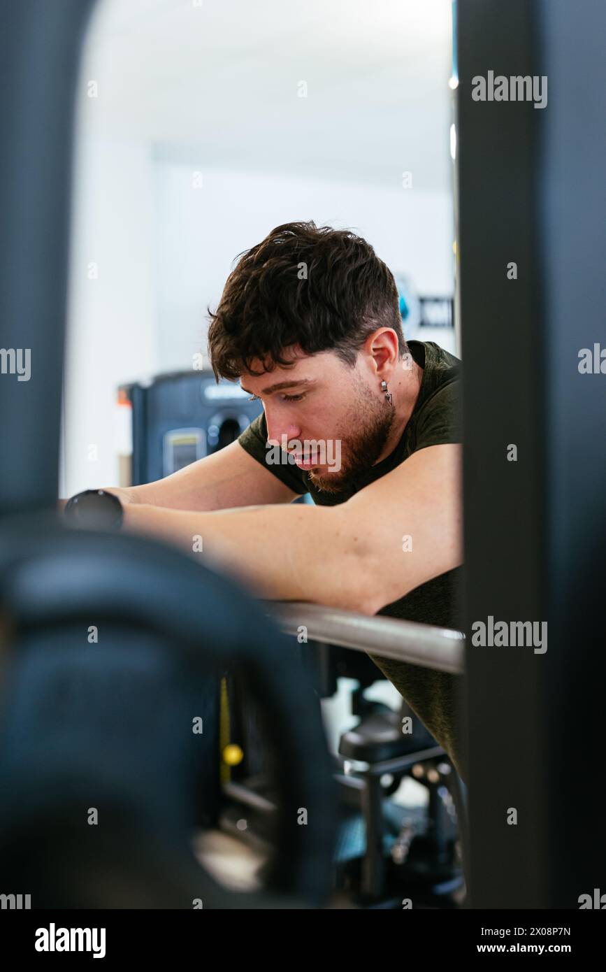 A concentrated young man leaning on gym equipment during a workout ...