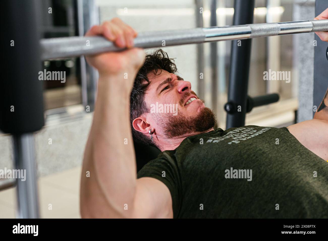 A focused young man lifts weights on a bench press at a gym, his ...