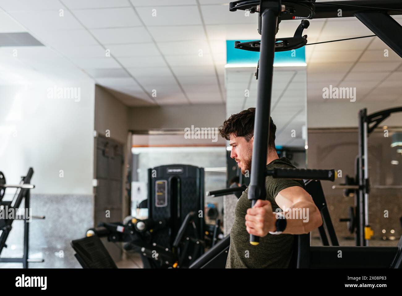 A focused young man is working out at the gym, using a cable machine ...
