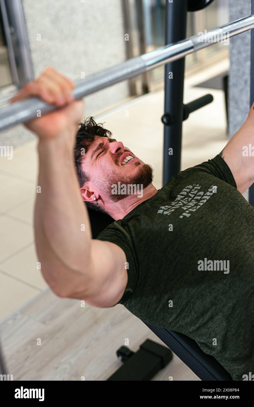 A young man is captured pushing through a challenging bench press ...