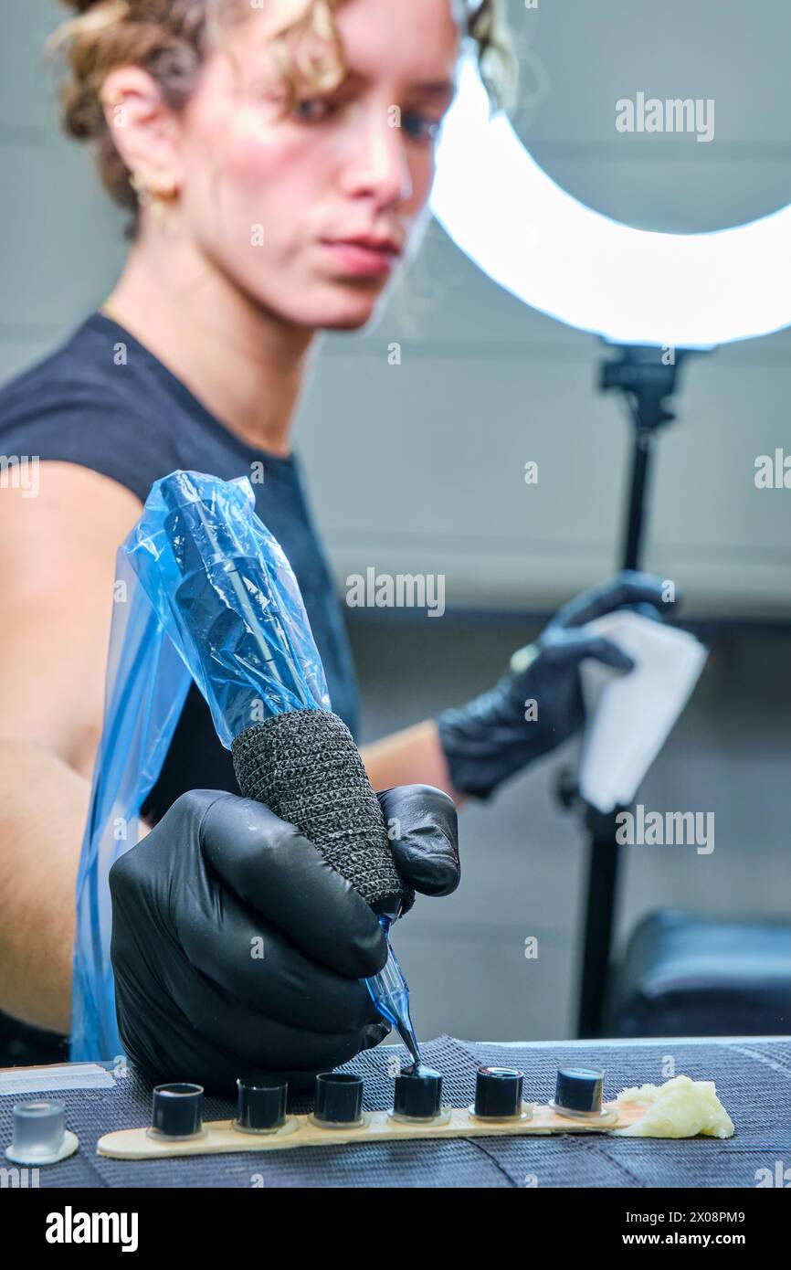 A female tattoo artist focuses on pouring ink into small caps before ...