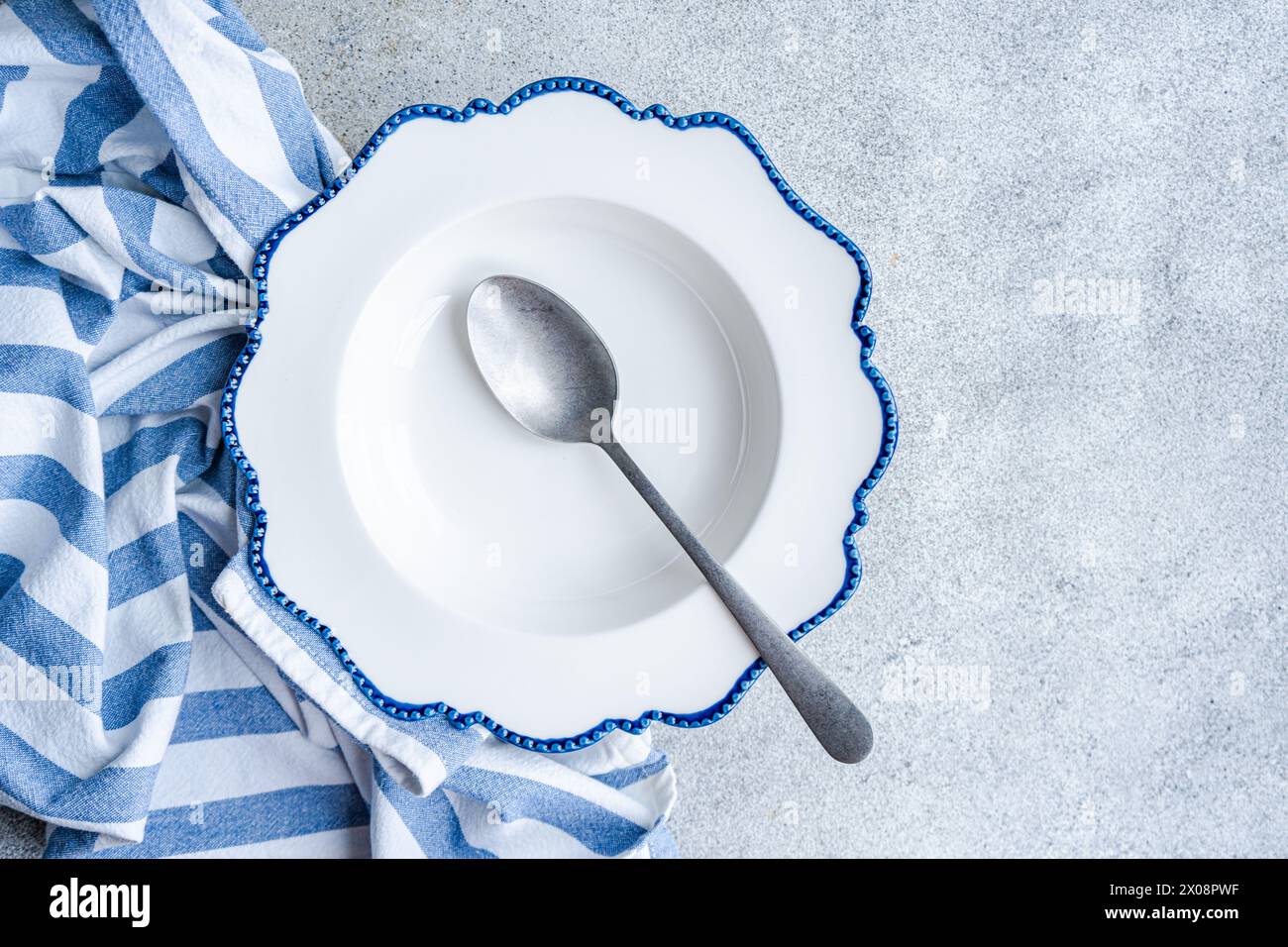 Elegant blue-edged plate with a spoon on a striped cloth over a stone ...