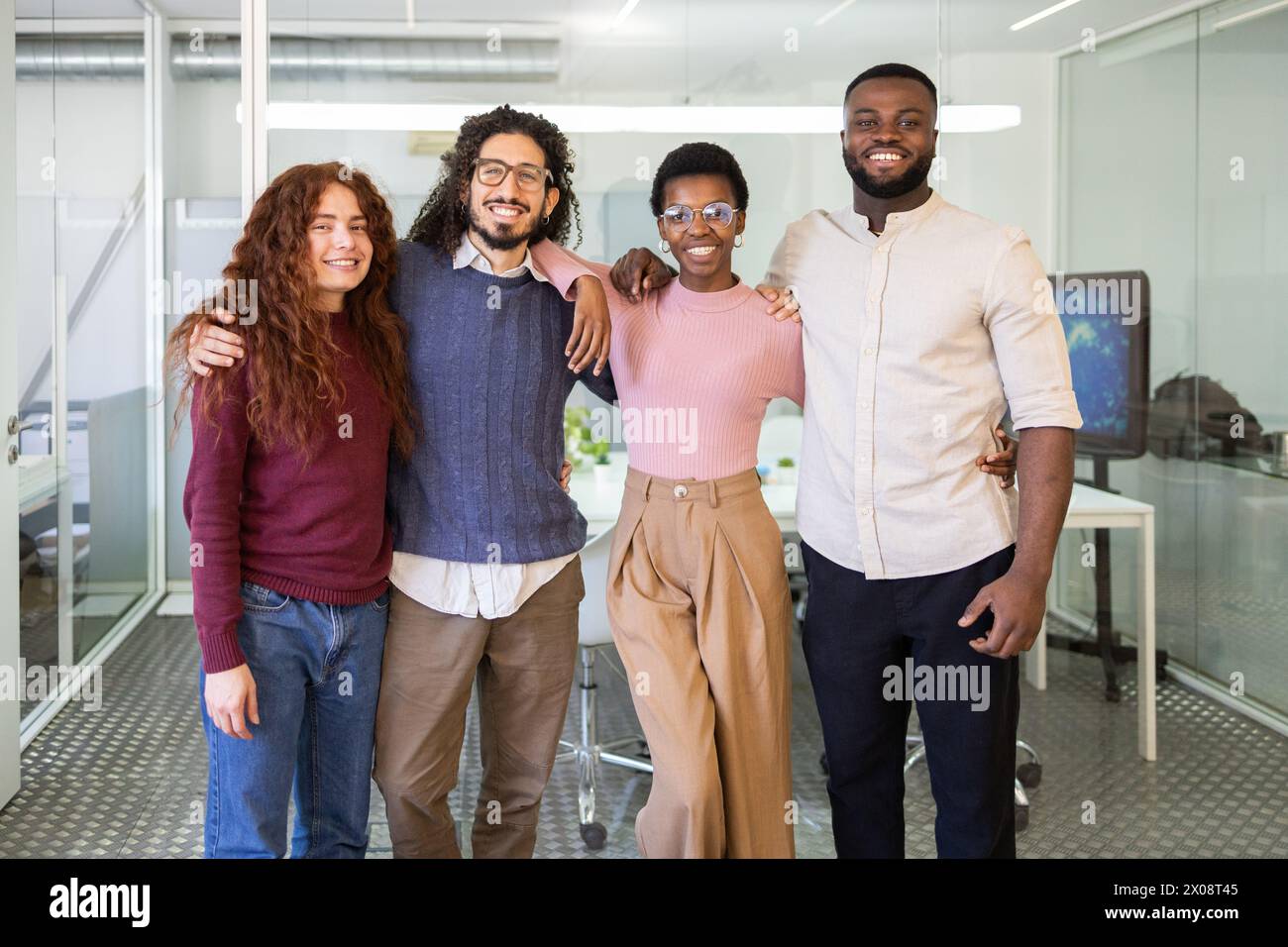 Four diverse colleagues sharing a friendly moment, standing with arms ...