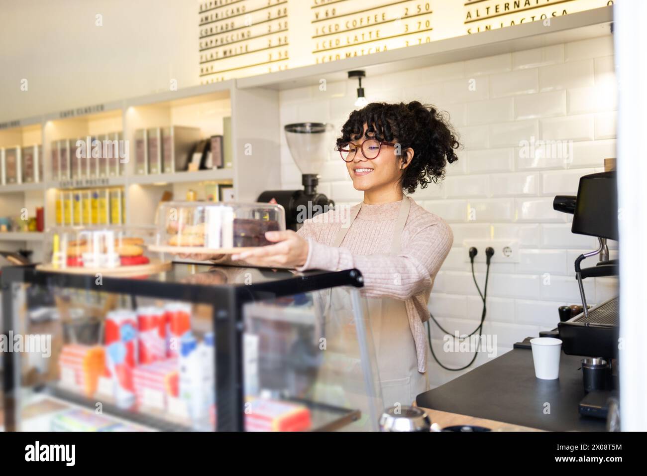 A smiling hispanic woman barista with curly hair standing behind a cafe ...