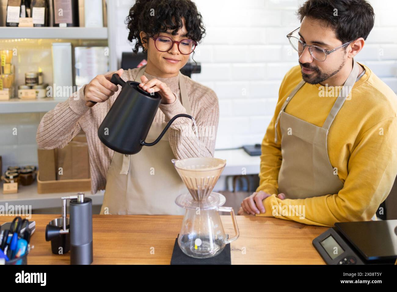 Two multiethnic baristas work together to brew pour-over coffee ...