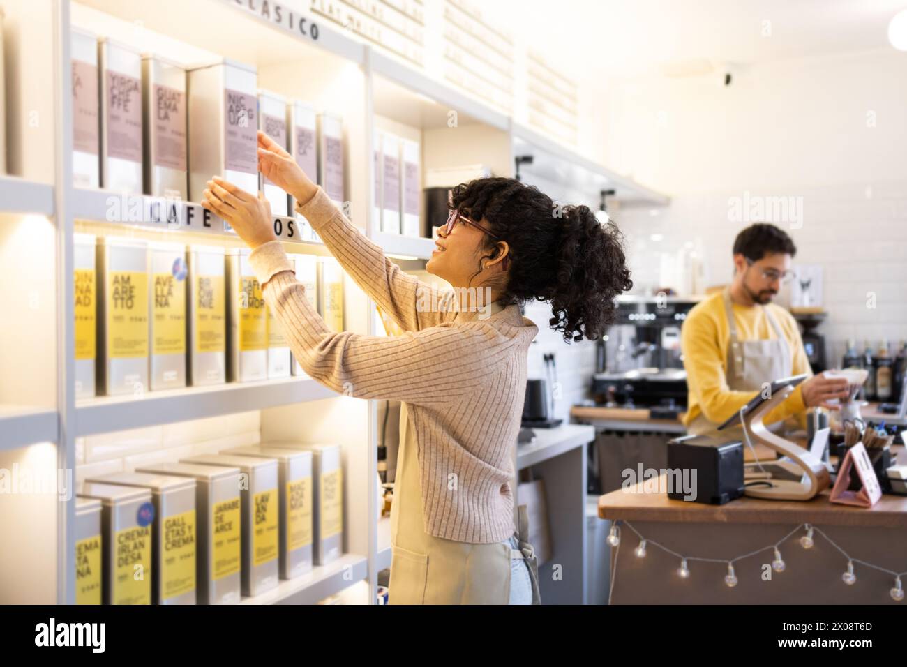 A happy female employee with curly hair is organizing product shelves ...