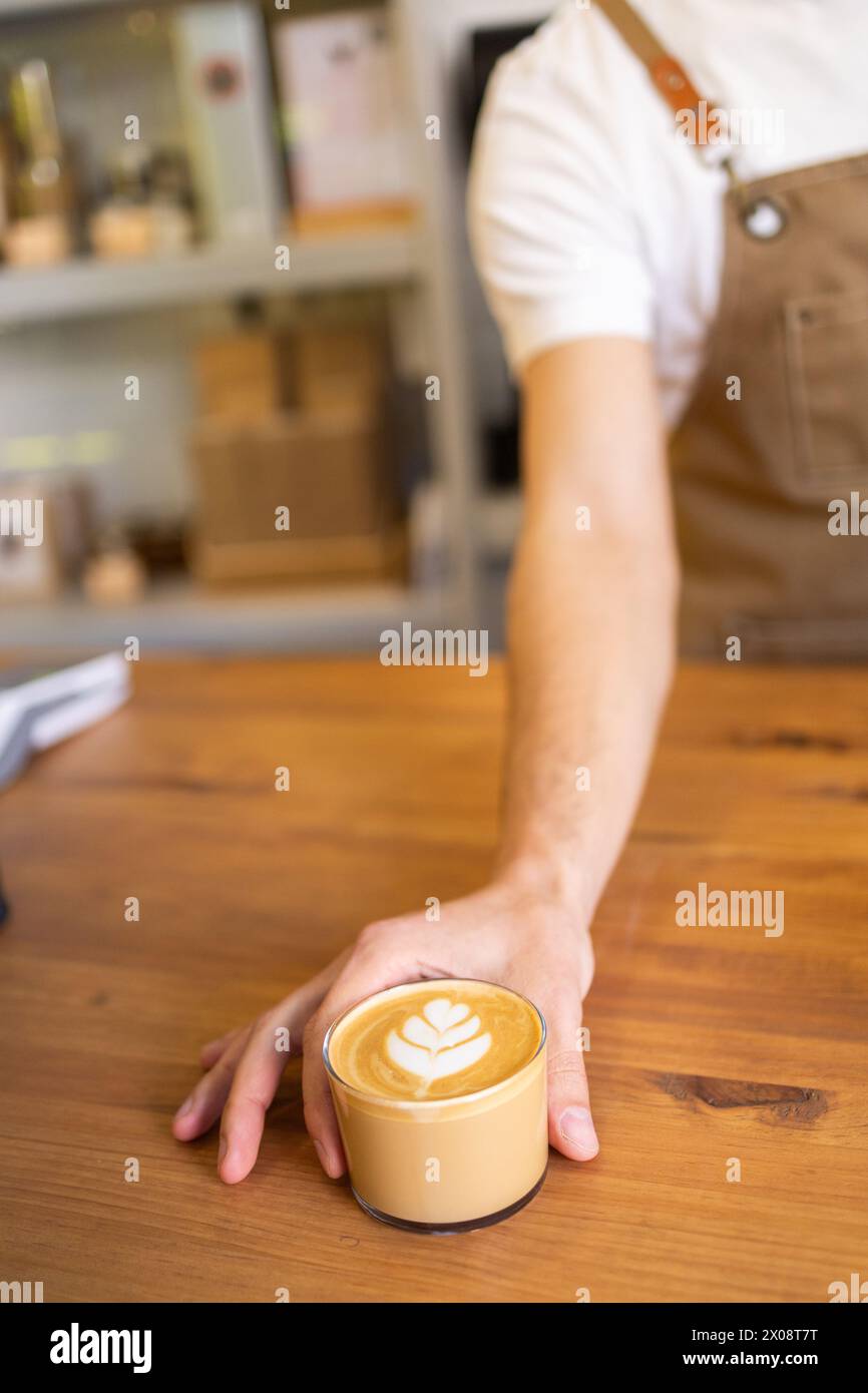 A barista's hand placing a freshly brewed latte with latte art on a ...