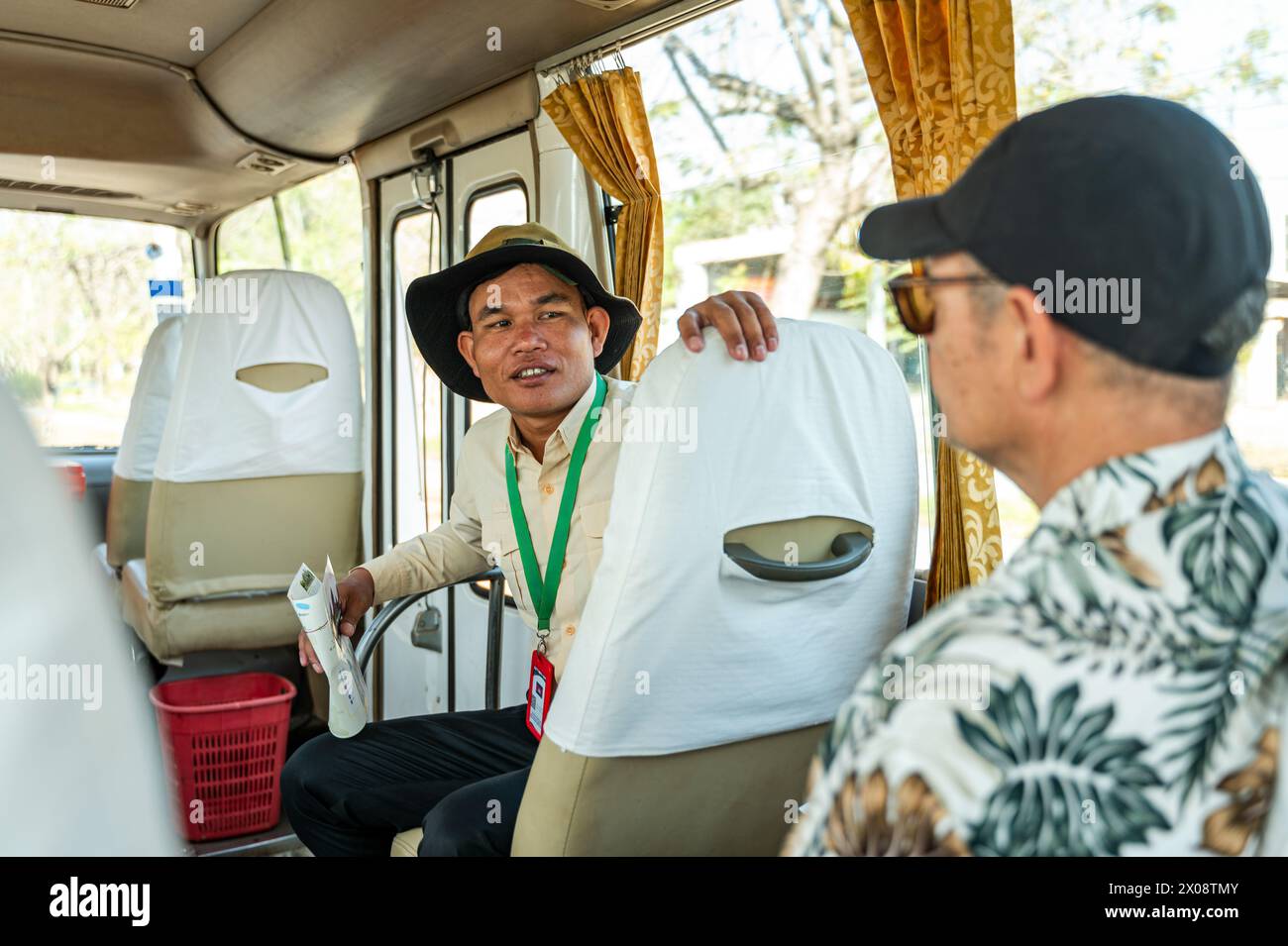 A tour guide in a hat talks with a passenger while holding brochures on ...