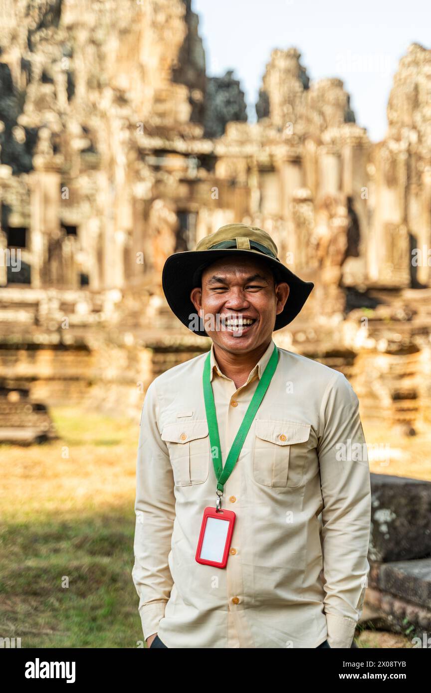 A cheerful local male guide wearing a safari hat and a lanyard smiles ...