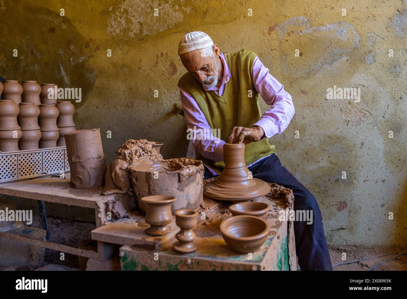 An experienced artisan shapes clay on a pottery wheel, surrounded by ...