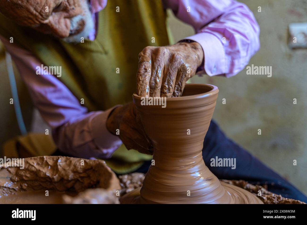 A skilled elderly male artisan shapes a clay pot on a pottery wheel ...