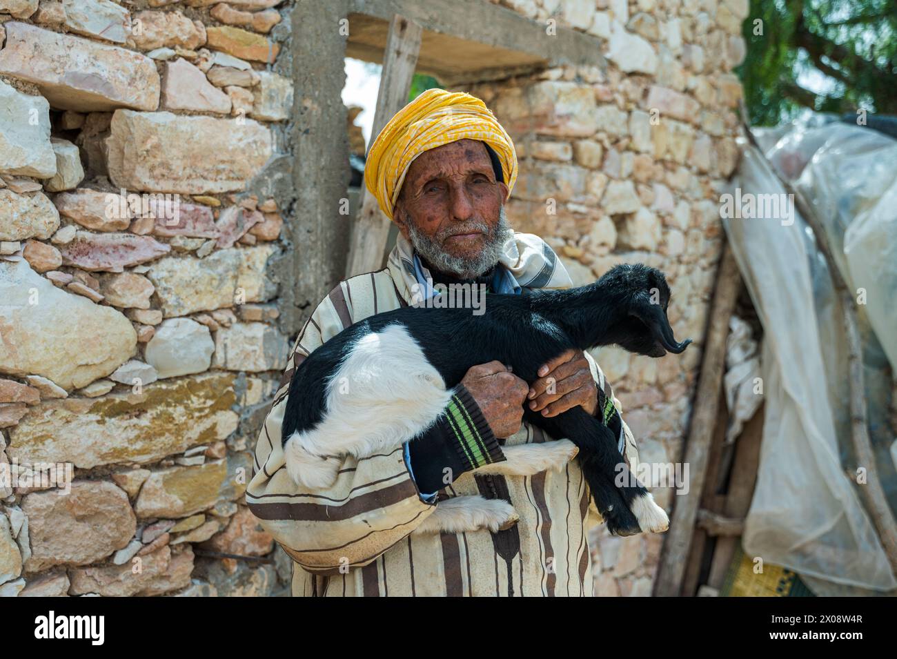 An elderly Moroccan man in traditional attire lovingly cradles a black ...