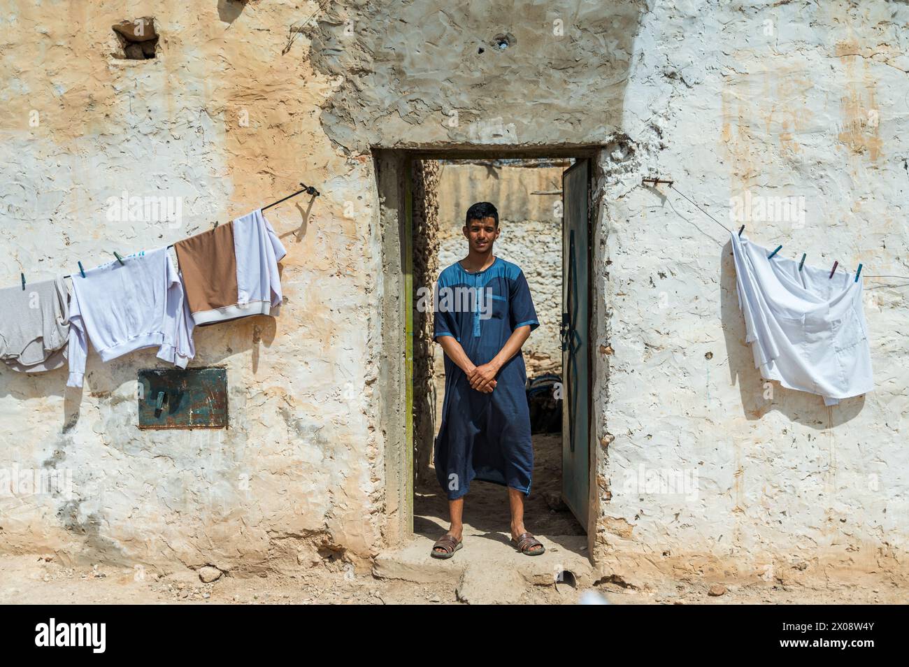 Man in traditional attire stands in a doorway with laundry drying ...