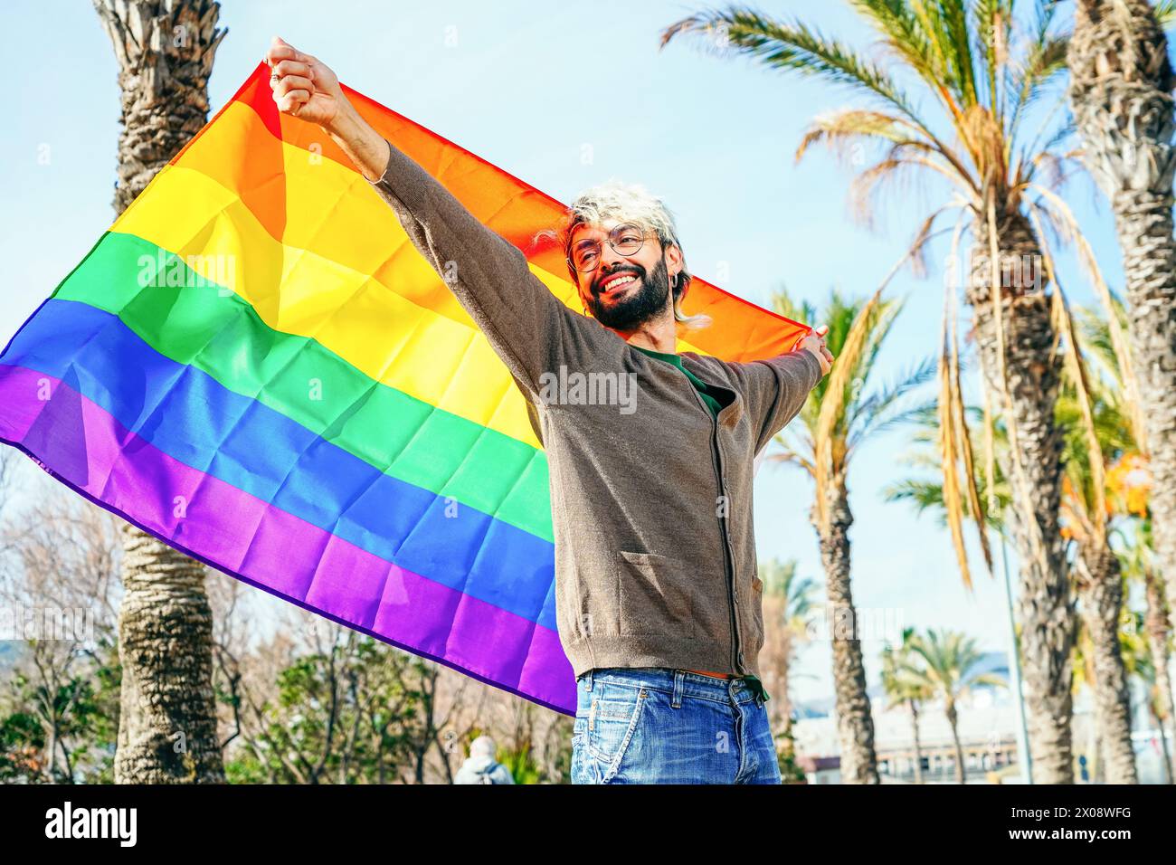 A person exudes joy while holding up a large rainbow pride flag ...