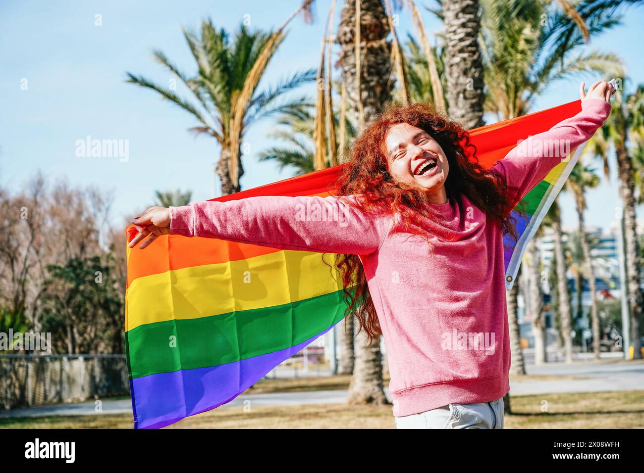 A joyful person with flowing hair spreads their arms wide, the rainbow ...