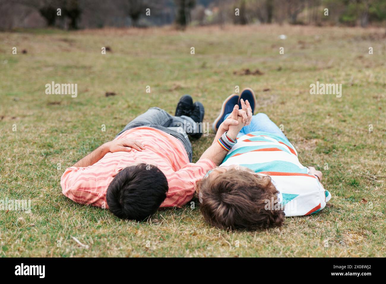 Lying side by side on a grassy field, a loving gay couple enjoys a ...