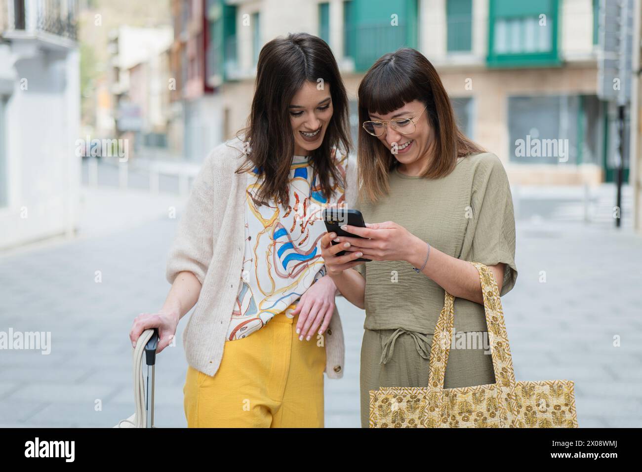 A joyful moment as two women share content on a phone, dressed in ...