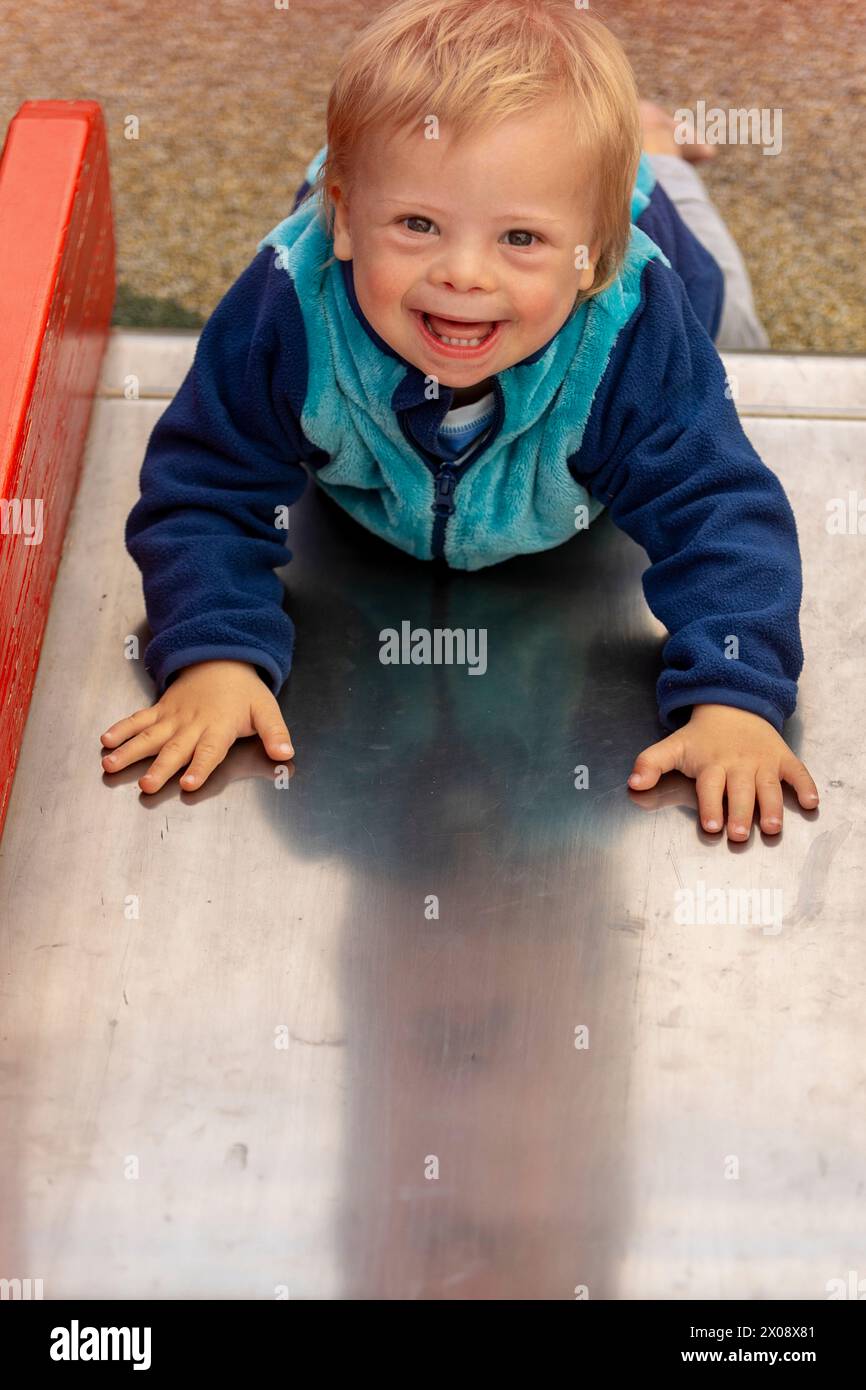 An adorable toddler with Down syndrome smiles brightly as they enjoy ...