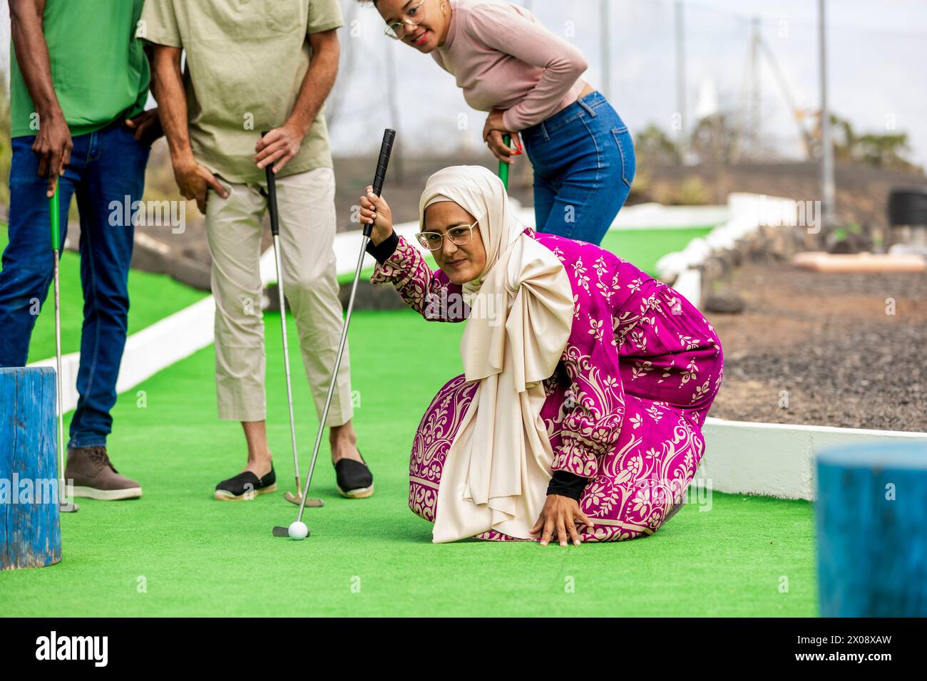 A multicultural group of friends share a laugh while playing mini golf ...