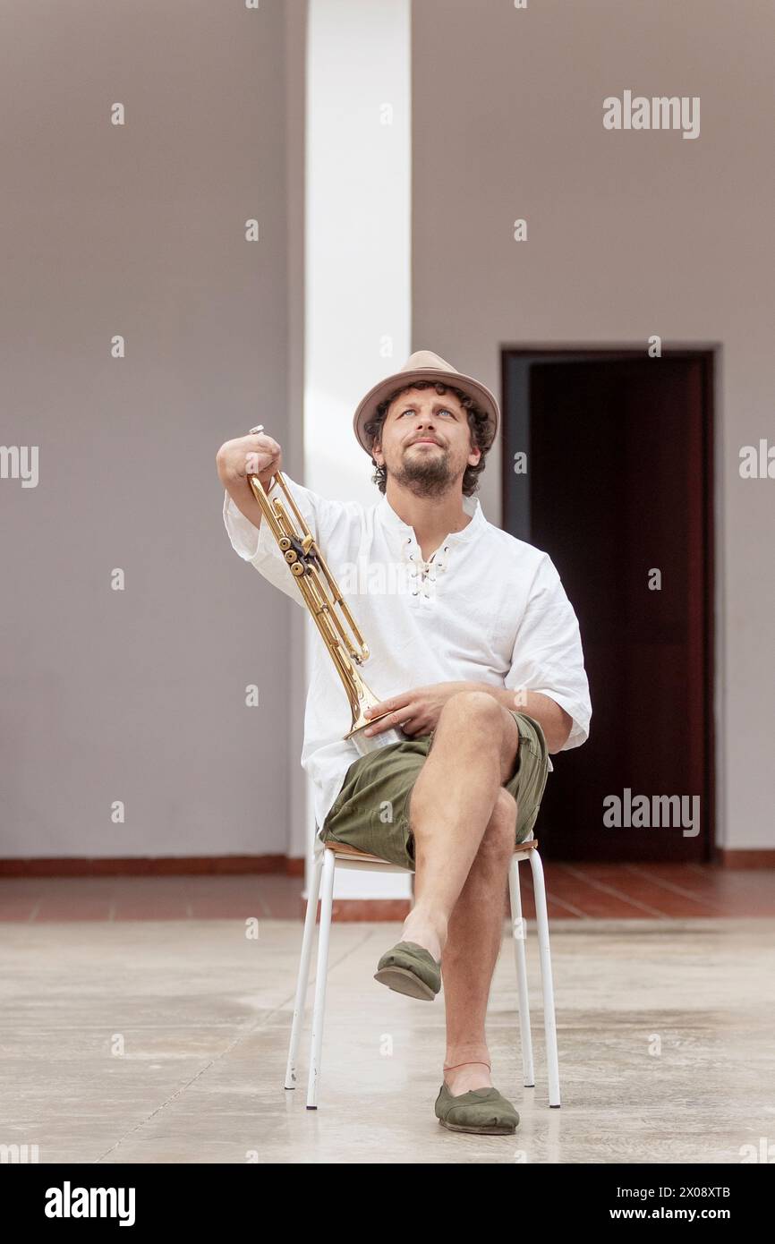 A man with one arm sits on a chair holding a trumpet, gazing upward ...