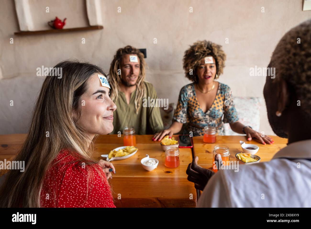 Group of diverse friends laughing and playing a sticky note guessing ...