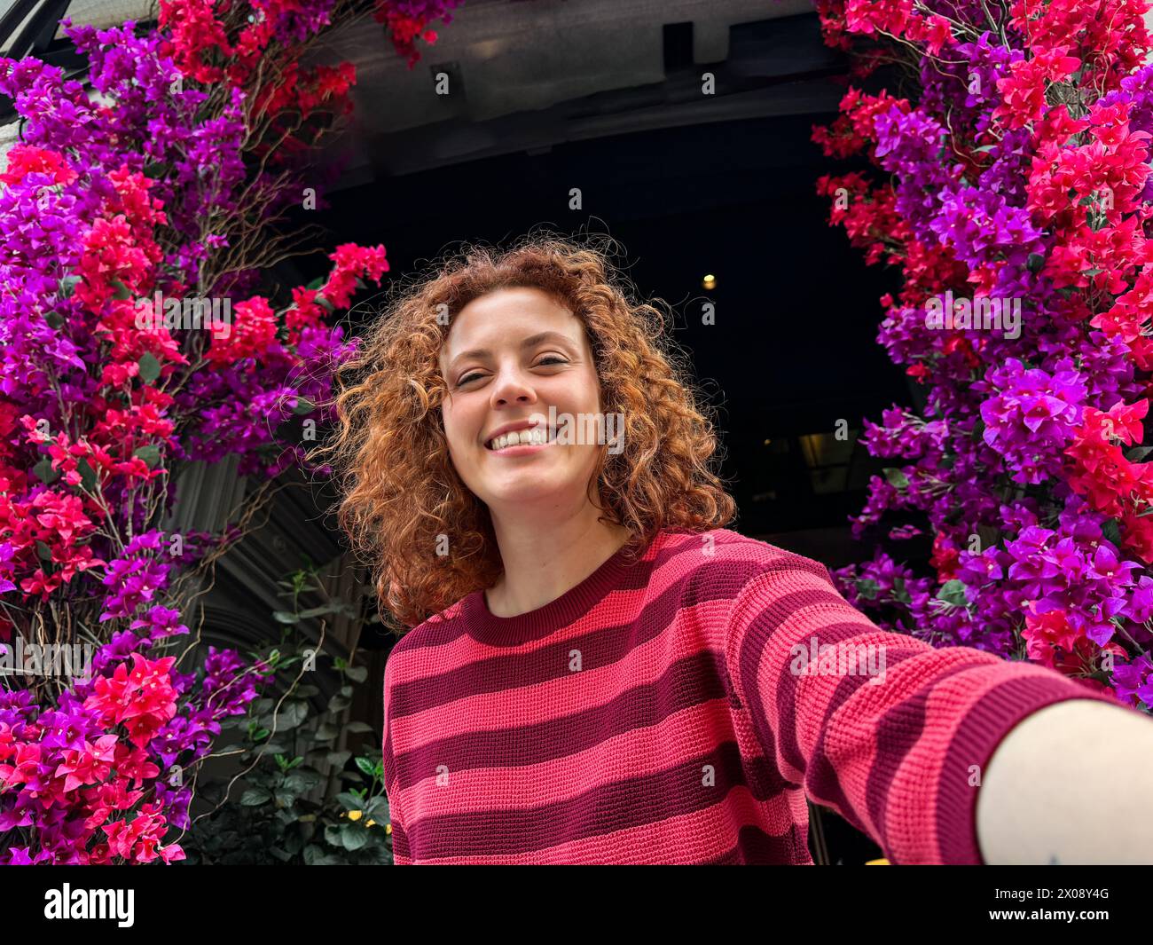 A cheerful young redhead woman with curly hair extends her arm to take ...