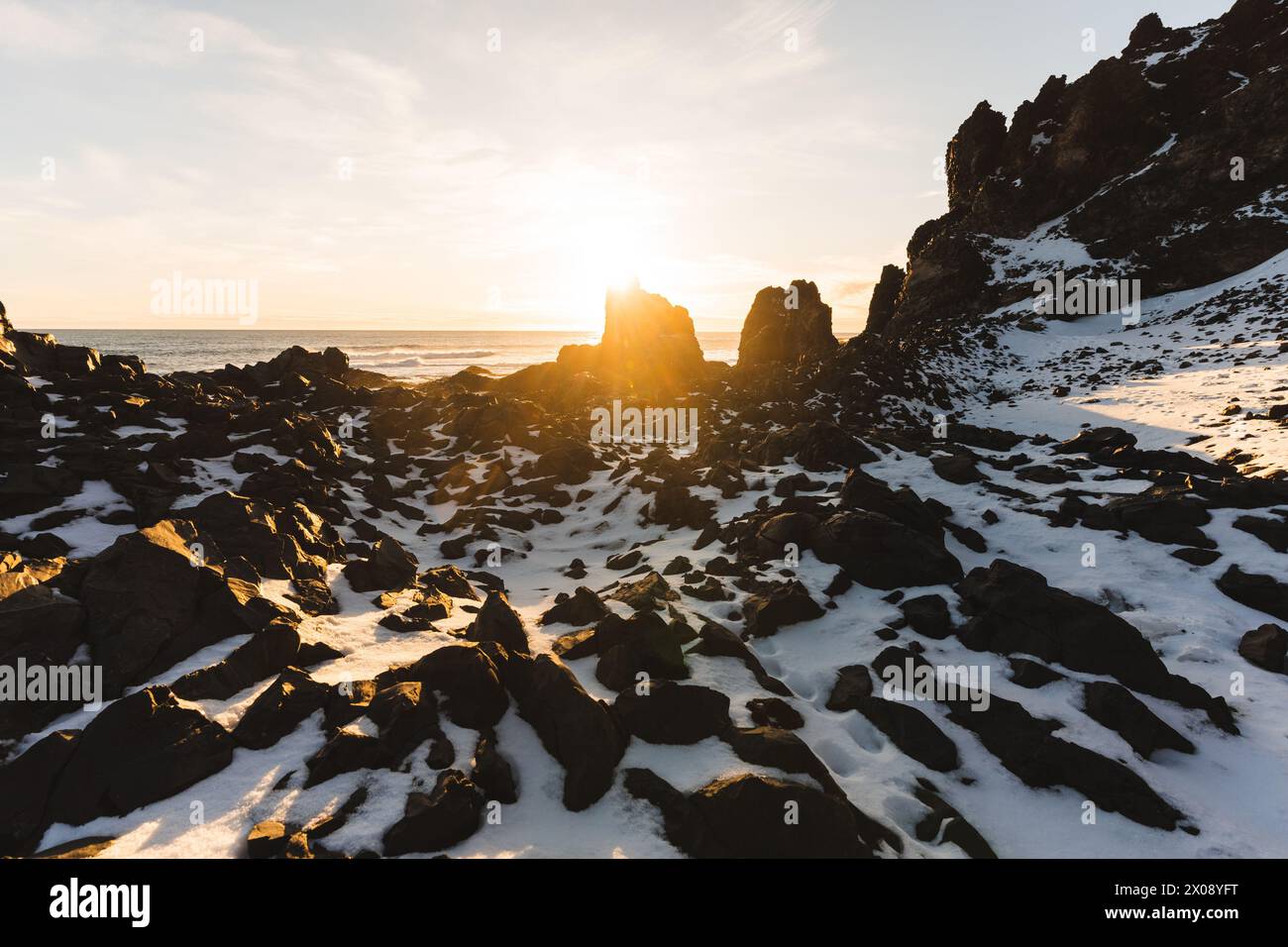 The setting sun casts a warm glow over the rugged, snow-spotted rocks ...