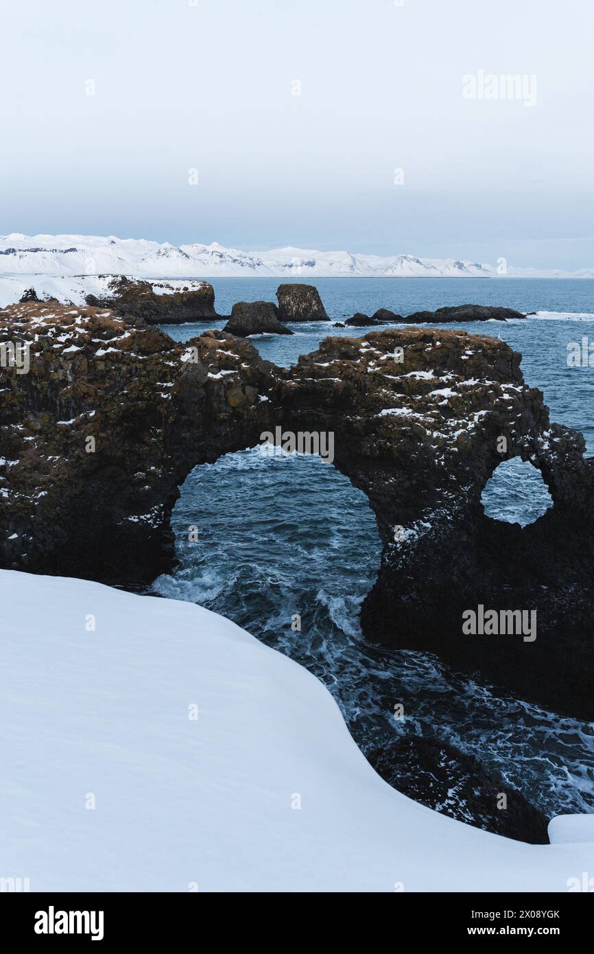The natural arch of volcanic rock stands amidst the snow and turbulent ...