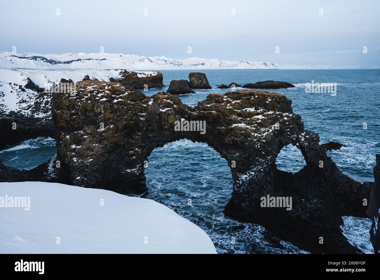 The natural arch of volcanic rock stands amidst the snow and turbulent ...