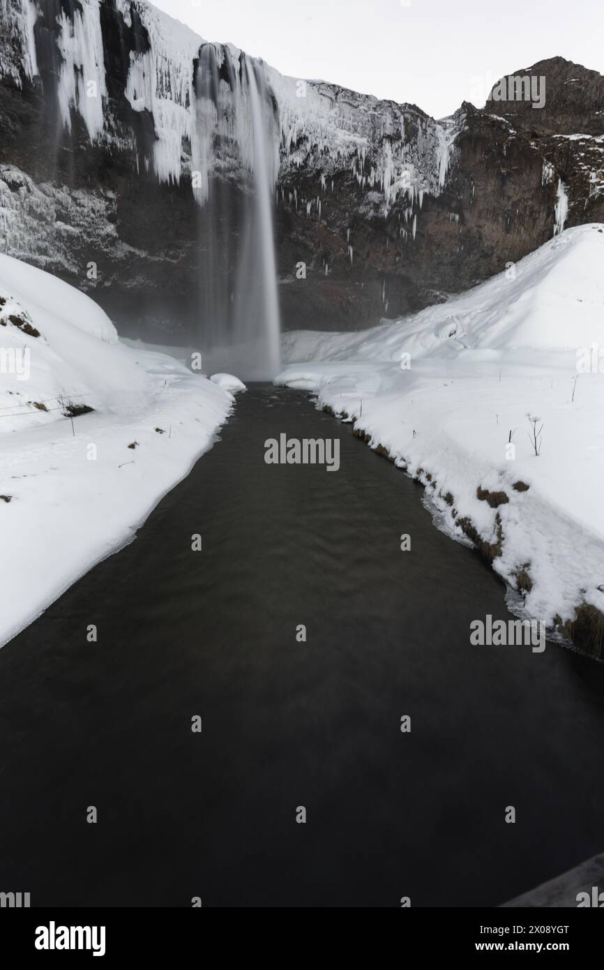 A majestic waterfall cascades in an icy embrace, framed by snow-draped ...