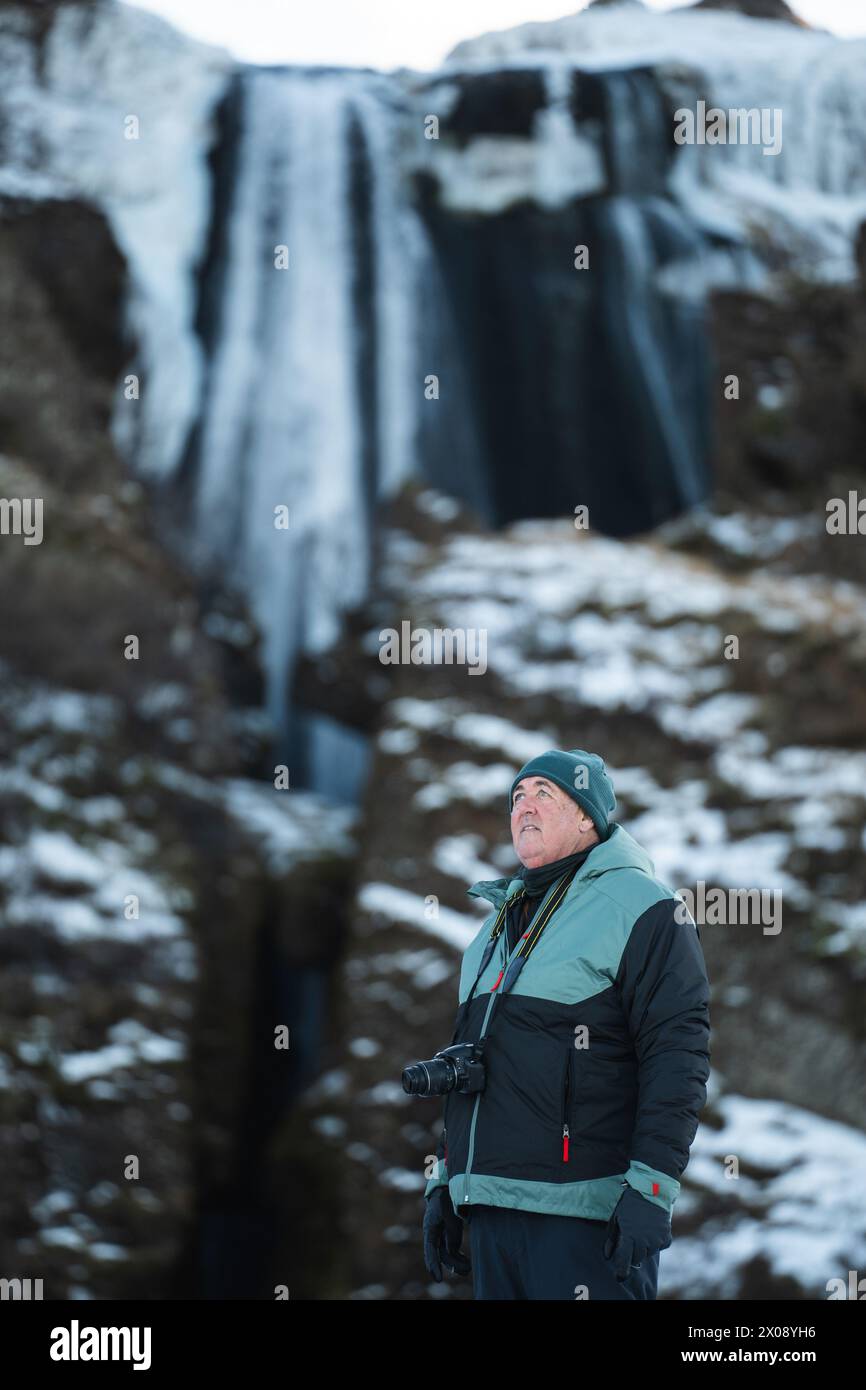 A rugged photographer in winter attire looks up in awe at the powerful ...