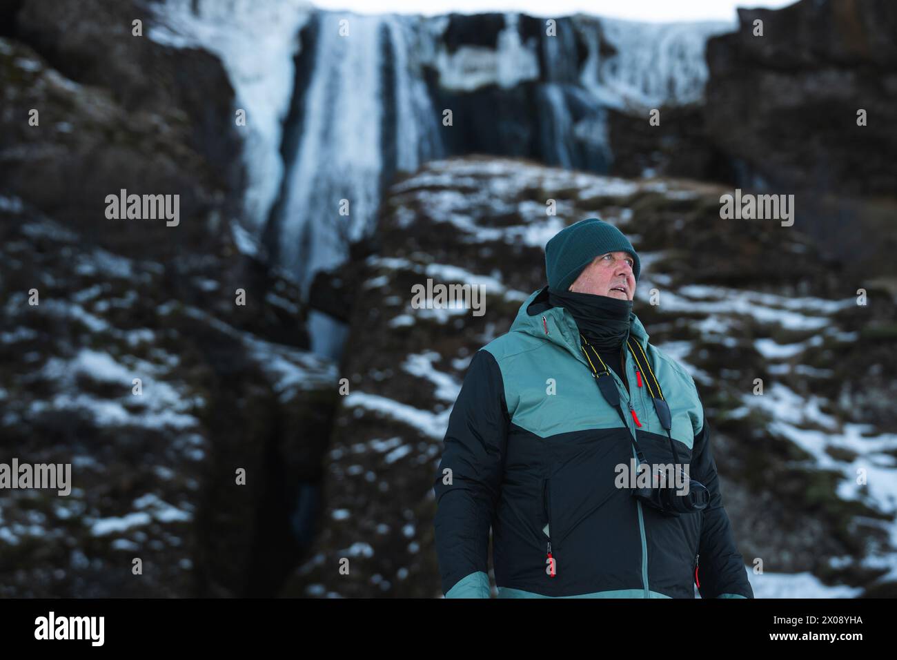 A rugged photographer in winter attire looks up in awe at the powerful ...
