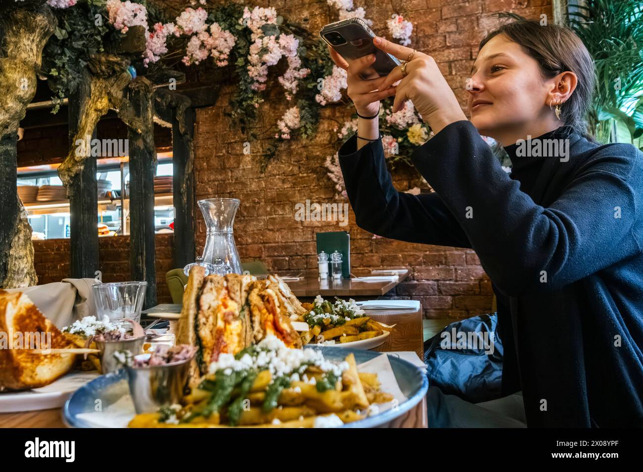 A young woman enjoys documenting her dining experience, taking a ...