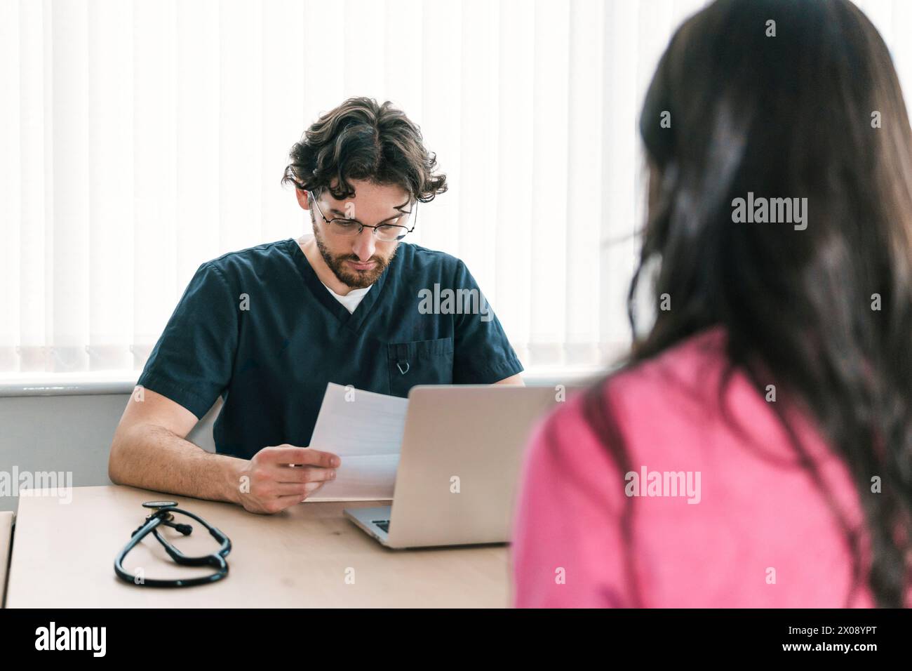 A doctor is intently reviewing documents during a patient appointment ...