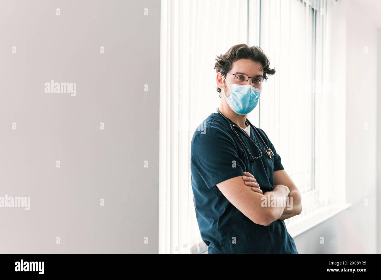 A vigilant male healthcare professional in navy scrubs wears a mask ...