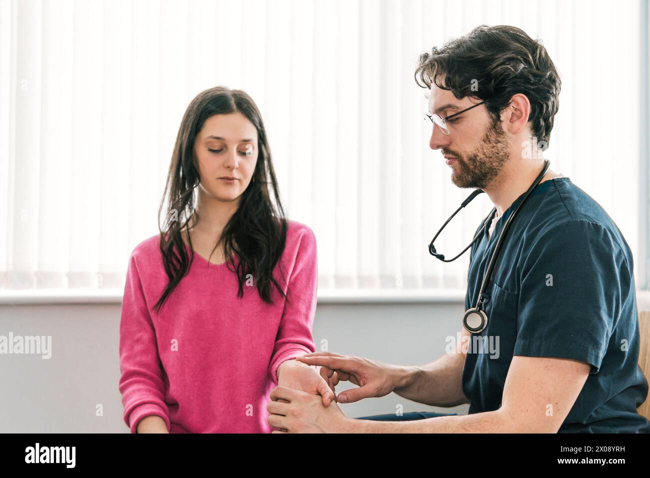 A doctor is attentively examining the elbow joint of a female patient ...