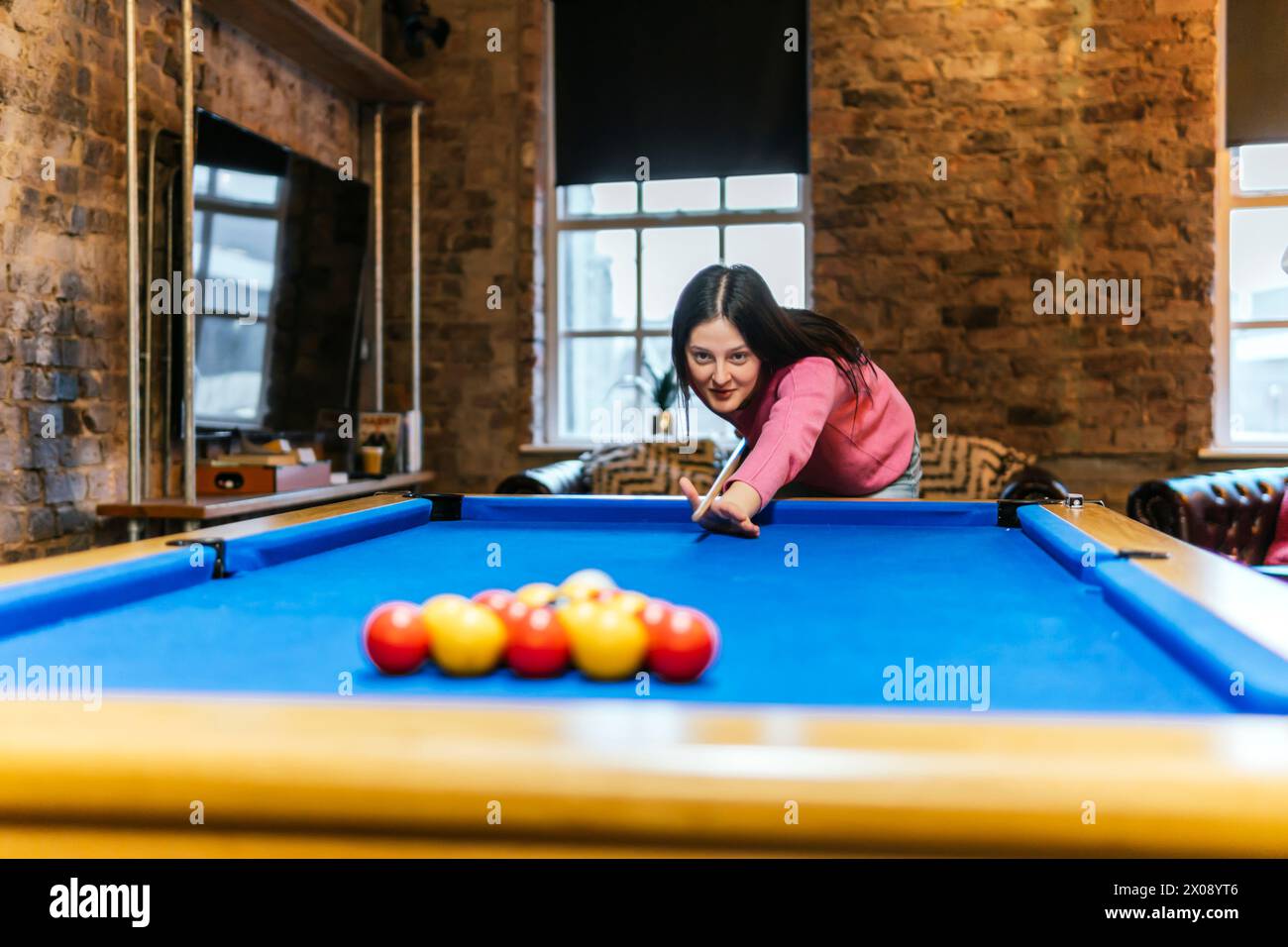 A young woman takes aim at the billiard balls during a friendly game of ...