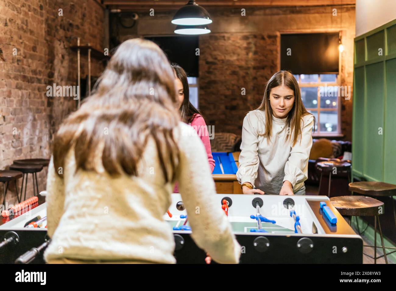A cheerful gathering of young women friends playing foosball in an ...