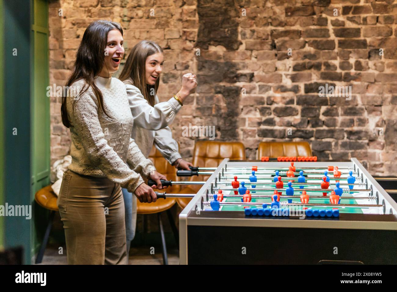Two young women share a joyful moment while playing table soccer in a ...