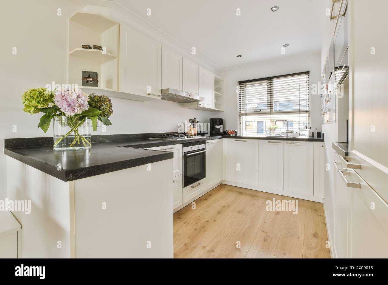 A bright modern kitchen featuring white cabinets, black countertops ...