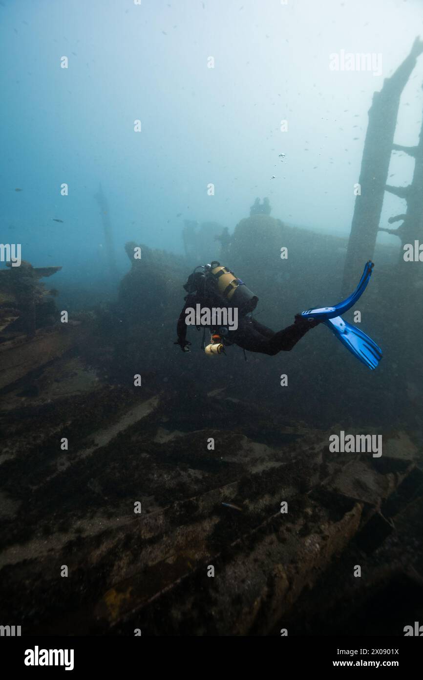 A scuba diver with fins and diving gear swims beside a sunken shipwreck ...