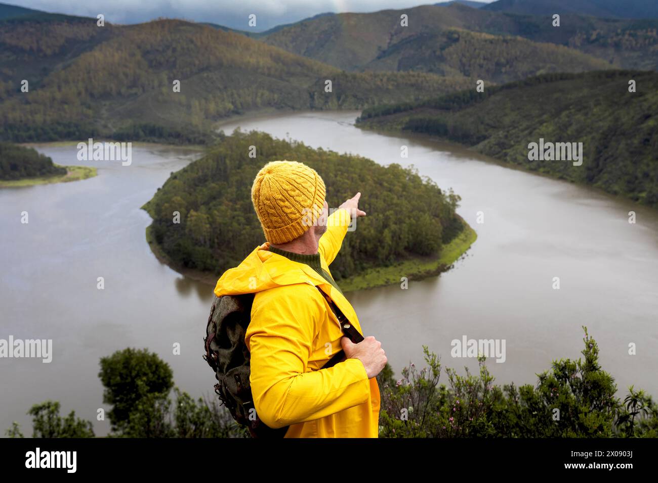 Side view of male traveler in a yellow jacket and beanie points at the ...