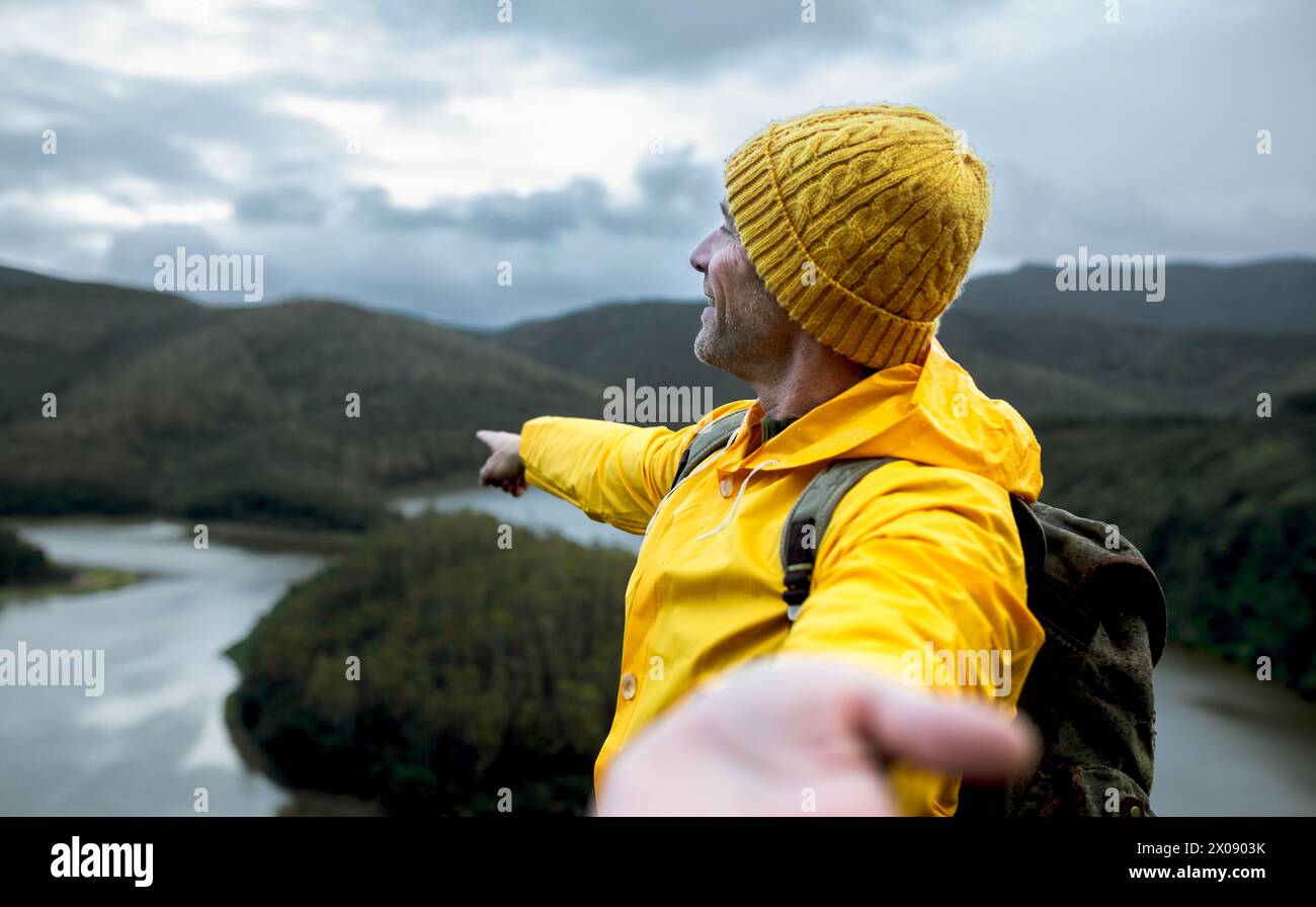 Side view of man in a yellow raincoat and woolen hat stands taking ...