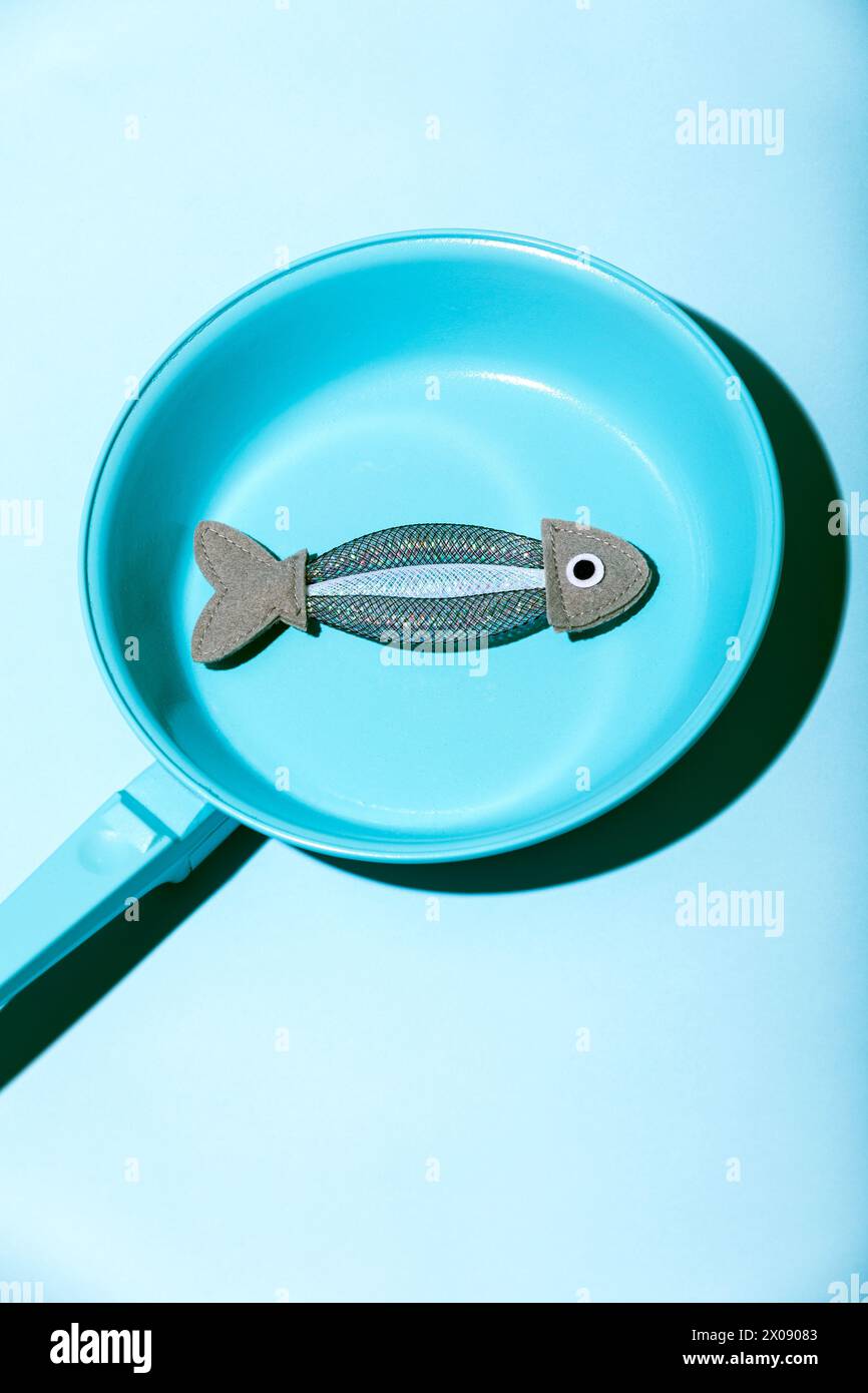 Minimalistic design of a cloth fish on a solid blue pan against a ...
