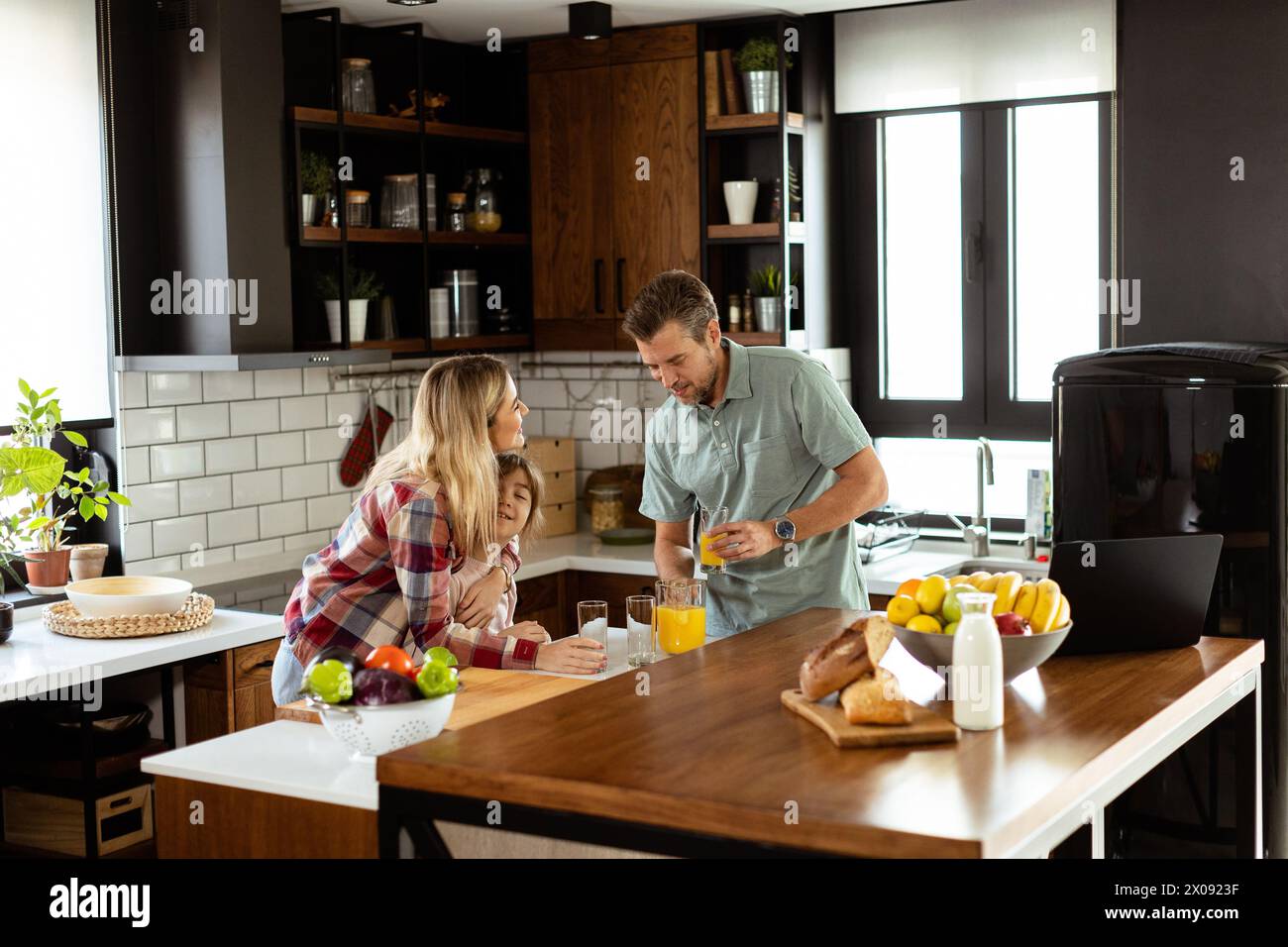 Young family chatting and preparing food around a bustling kitchen ...